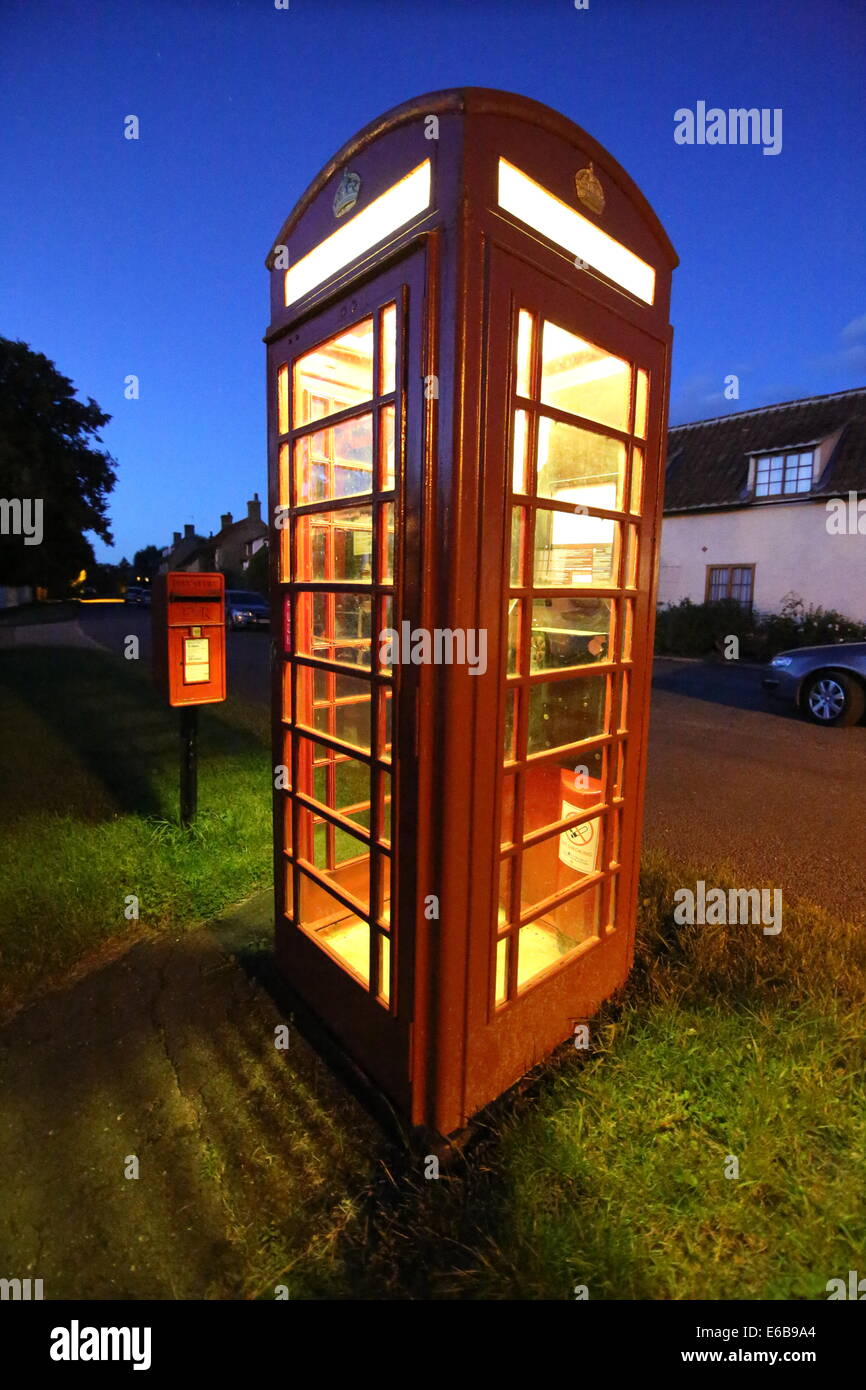 A traditional red telephone box at night in an English village, with a ...