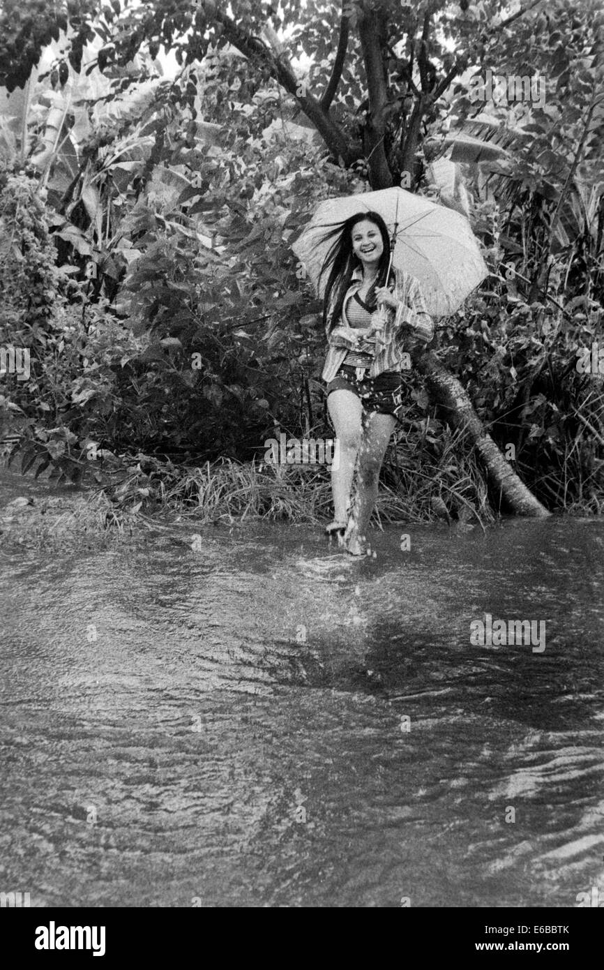 young woman with umbrella enjoying heavy rain during a monsoon downpour ...