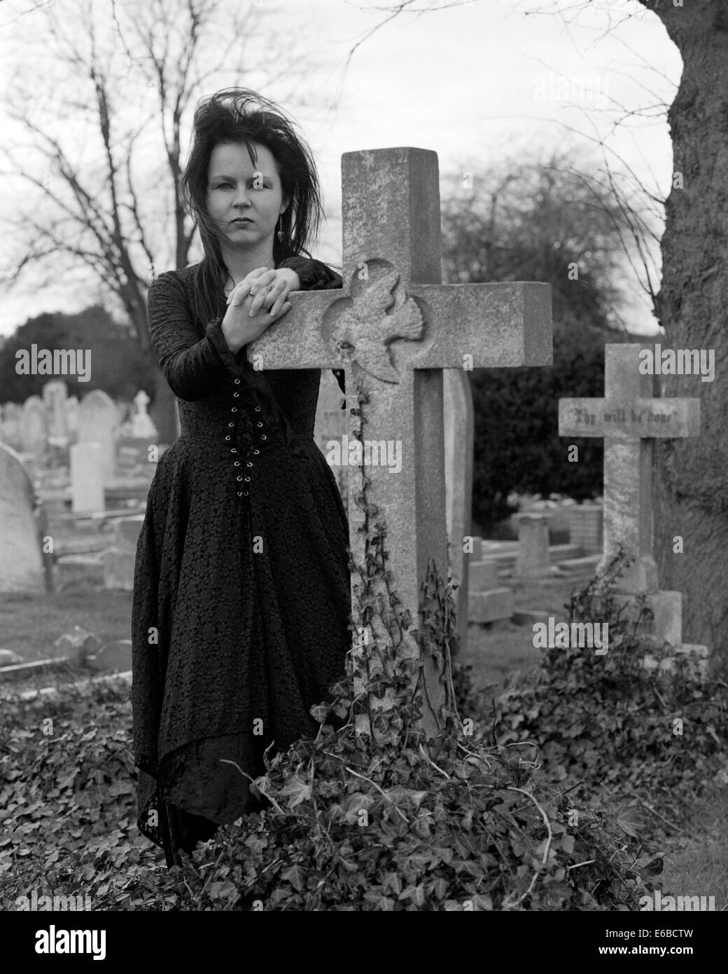 young fashionable goth dressed in black in a church graveyard ...