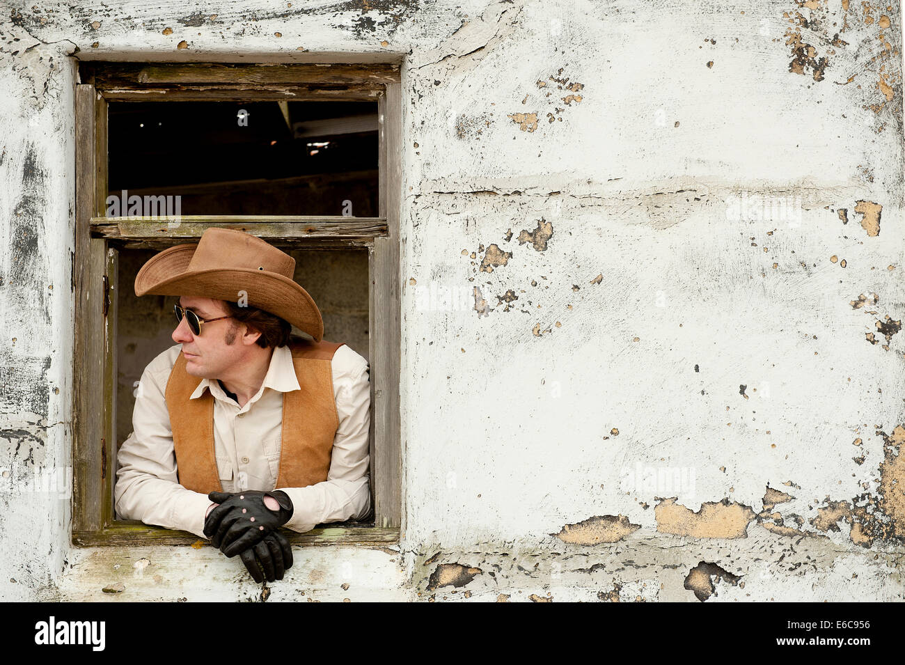 Modern day cowboy, looking out of the window of a derelict building ...
