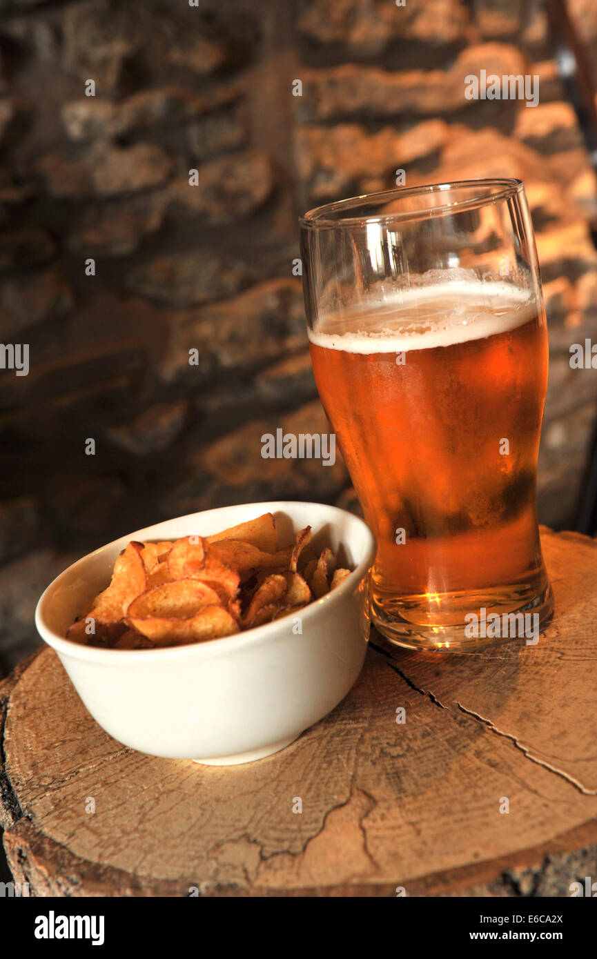 Kettle crisps in a bowl next to a real ale on a rustic log in a ...