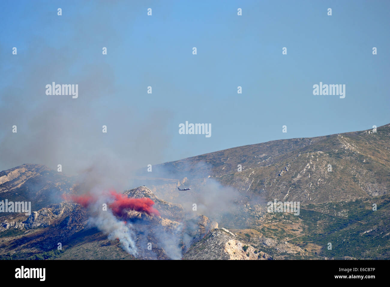 Plane dropping fire retardant on a bush forest wildfire on hills next ...