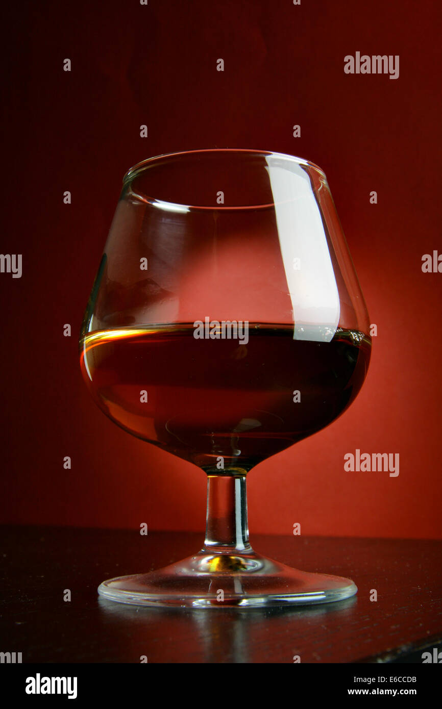 Glass of cognac close-up over deep red background Stock Photo - Alamy