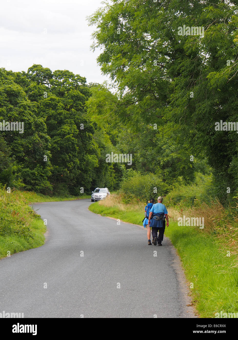 Hikers walking at the side of a country lane with no pavement as a car ...