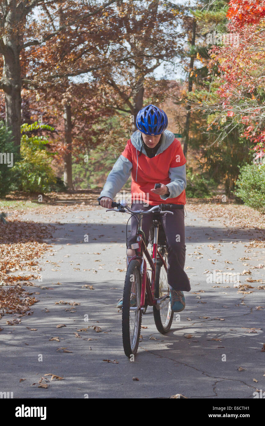 Young woman texting on her cell phone while riding a bike and not ...