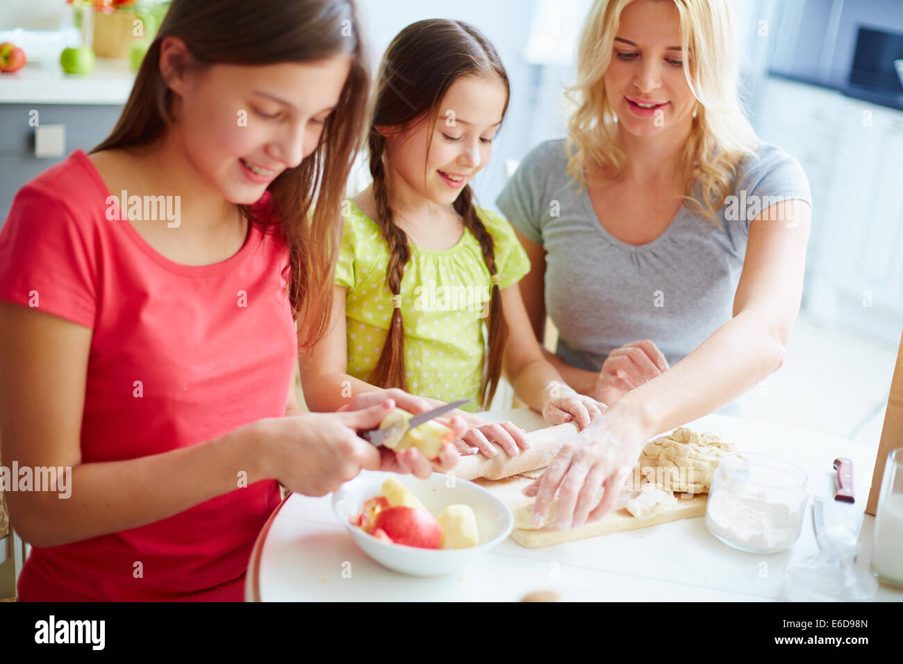 Two daughters making an apple pie with their mother Stock Photo - Alamy