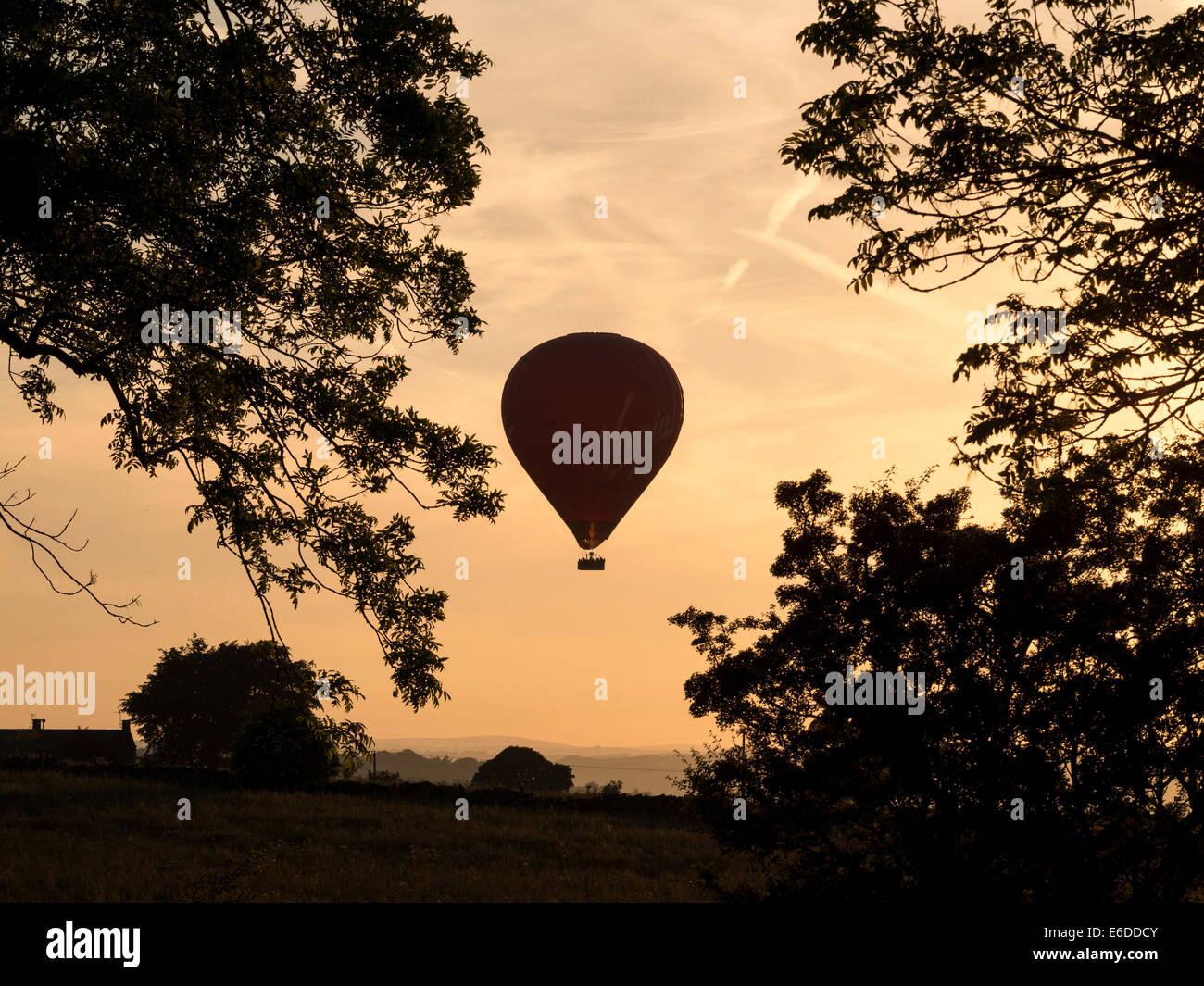 A balloon carrying passengers comes in to land over fields at dusk ...