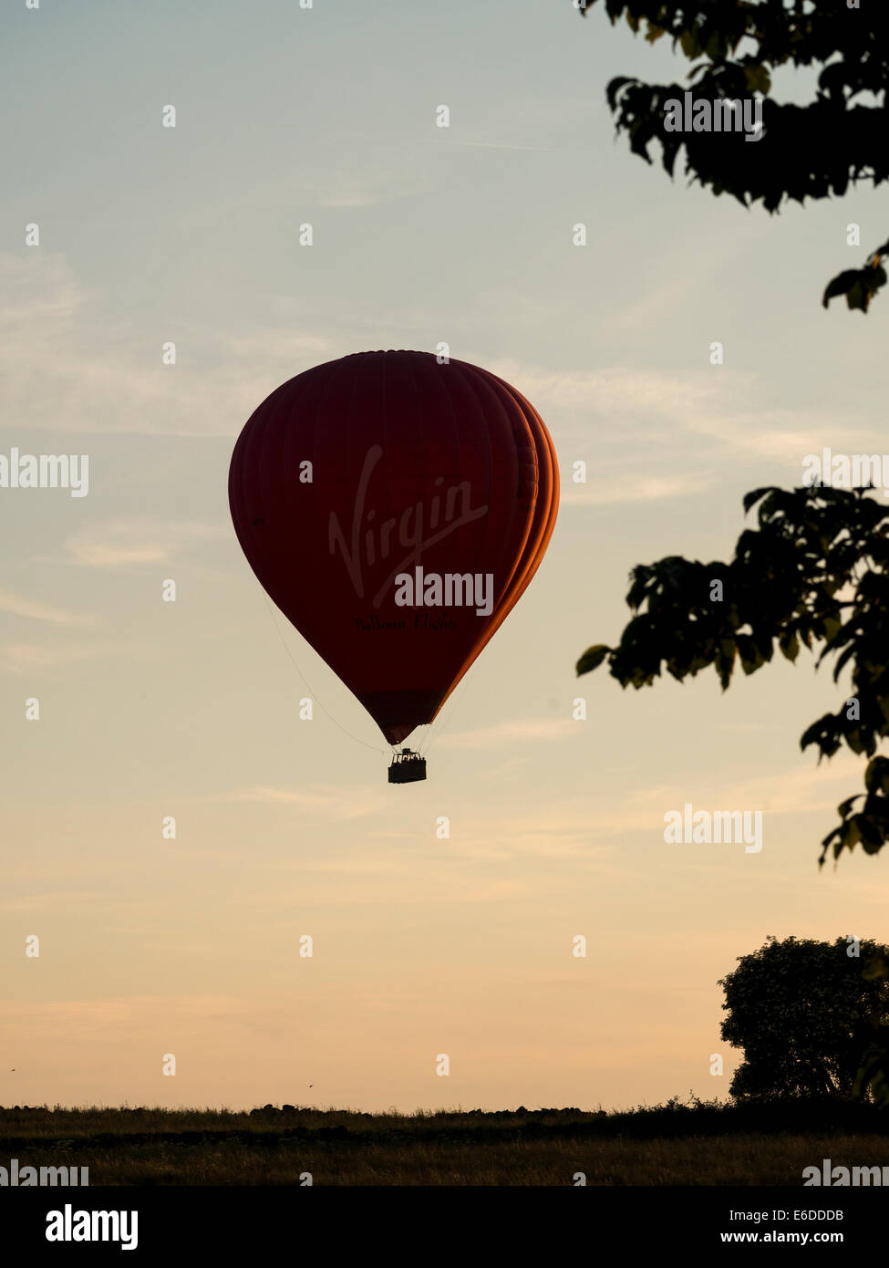 A balloon carrying passengers comes in to land over fields at dusk ...