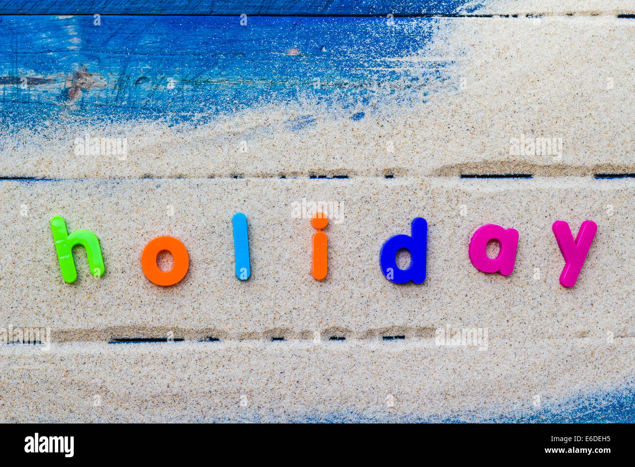 The word holiday laid sand and blue board Stock Photo - Alamy