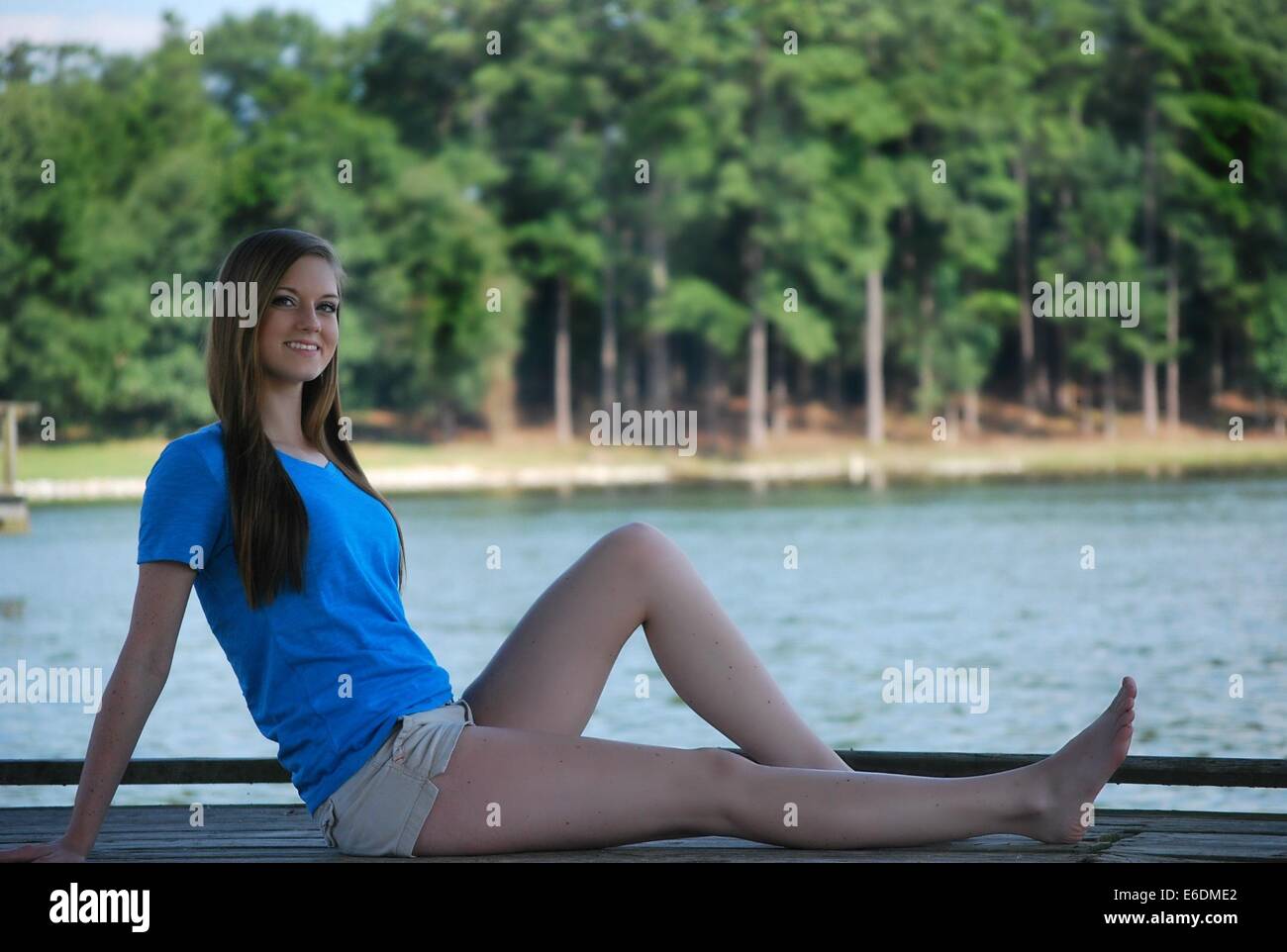 A girl sits happily on a dock near a lake, enjoying the summer weather ...