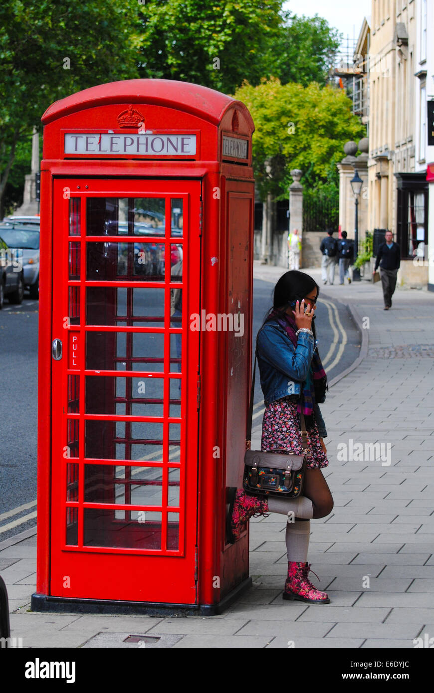 Teenage student girl on a mobile telephone outside a red telephone box ...