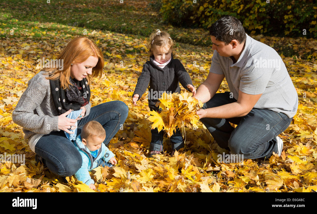 Happy young family in fall making a walk and play with maple leaves ...