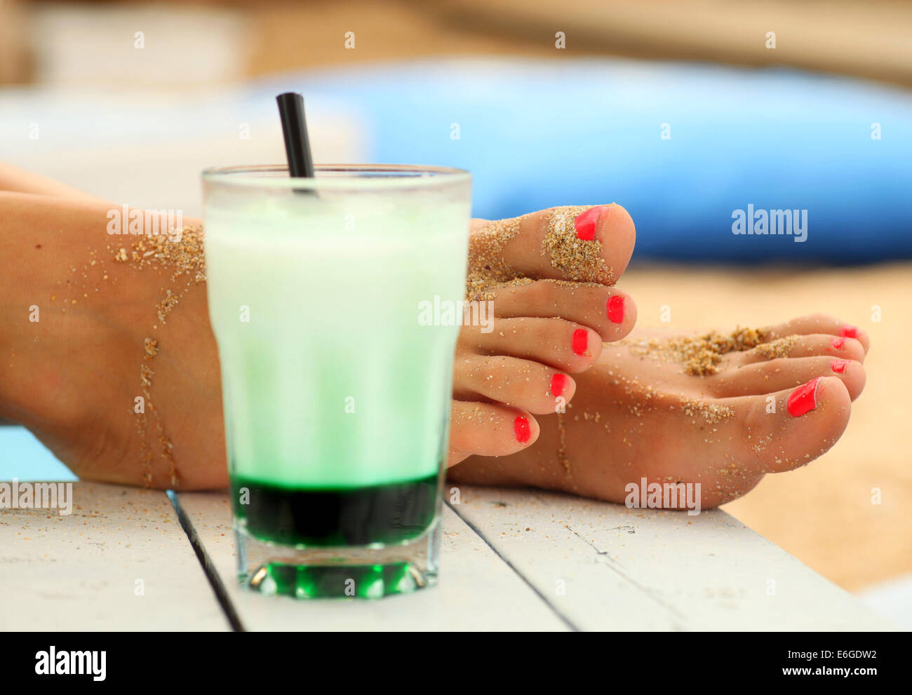 Cocktail with milk and mint liquor and feet in an exotic beach. Focus ...