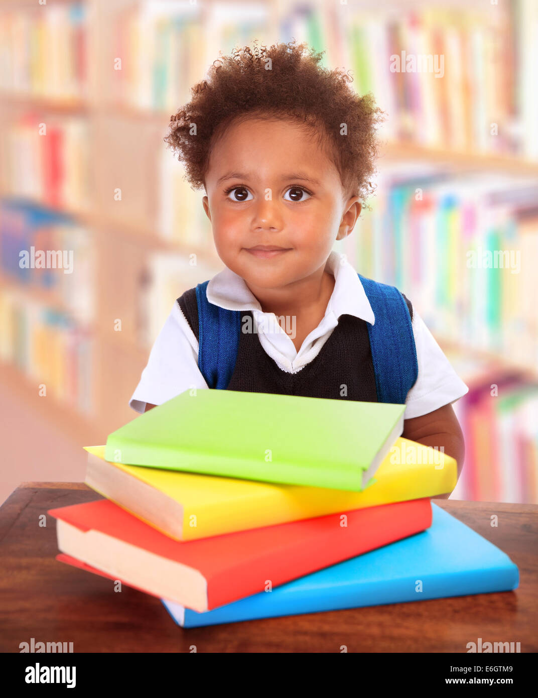Portrait of little African schoolboy sitting in library and reading ...