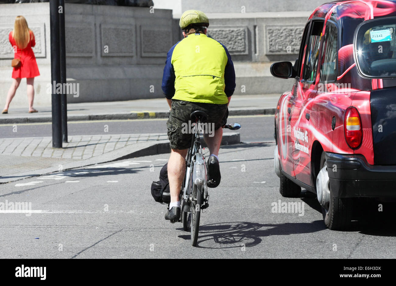 A cyclist riding a bicycle in London, alongside a taxi. Rear view of a ...
