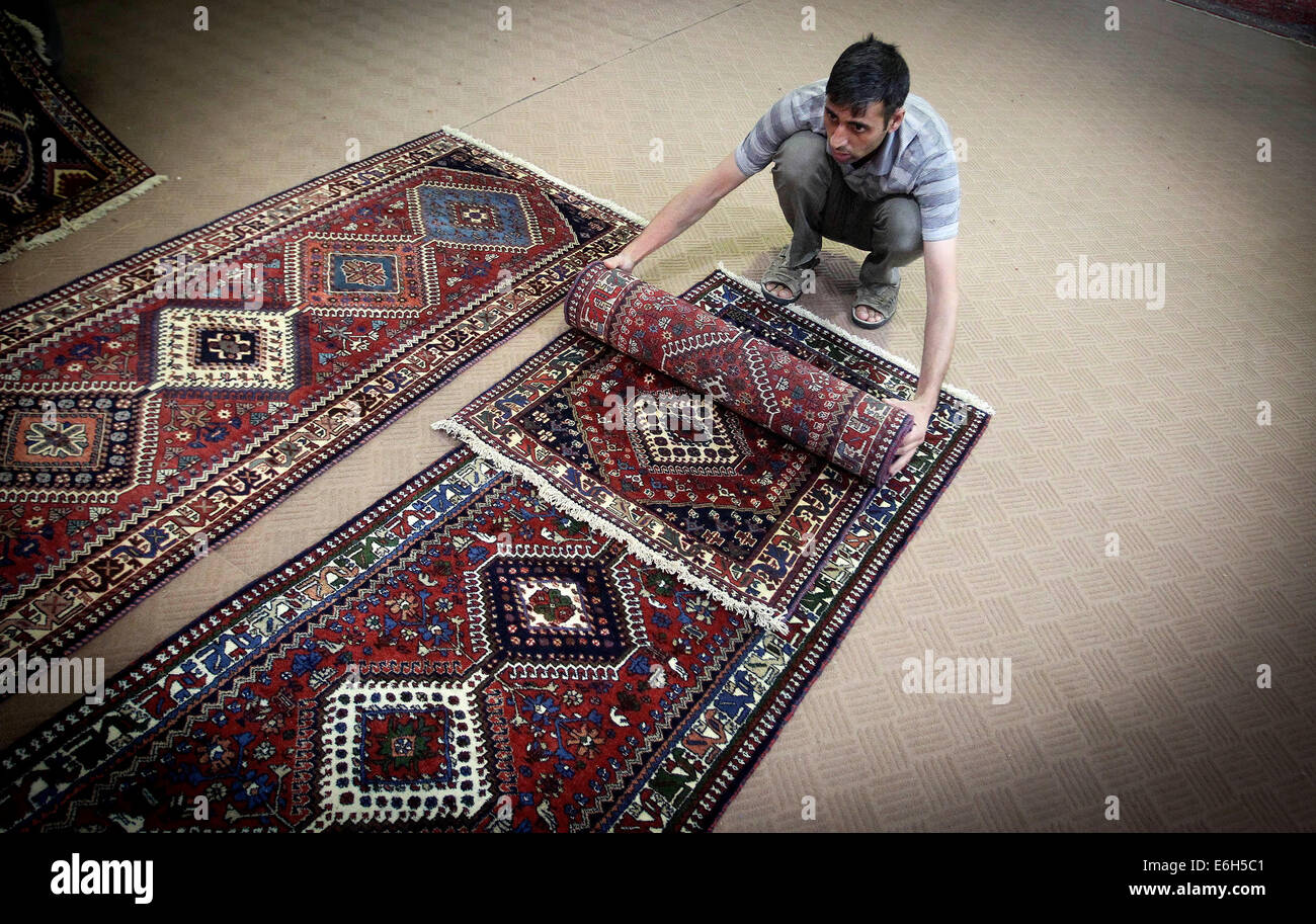 Tehran, Iran. 23rd Aug, 2014. A worker shows carpets to visitors during ...
