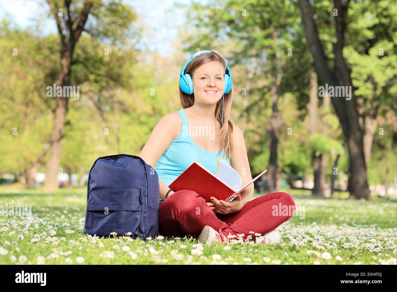 Female student studying on campus seated in a meadow full of flowers ...