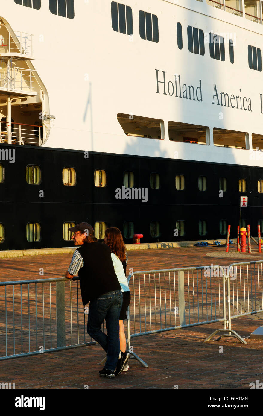 A couple leaning against the railing looking at a large cruise ship in ...