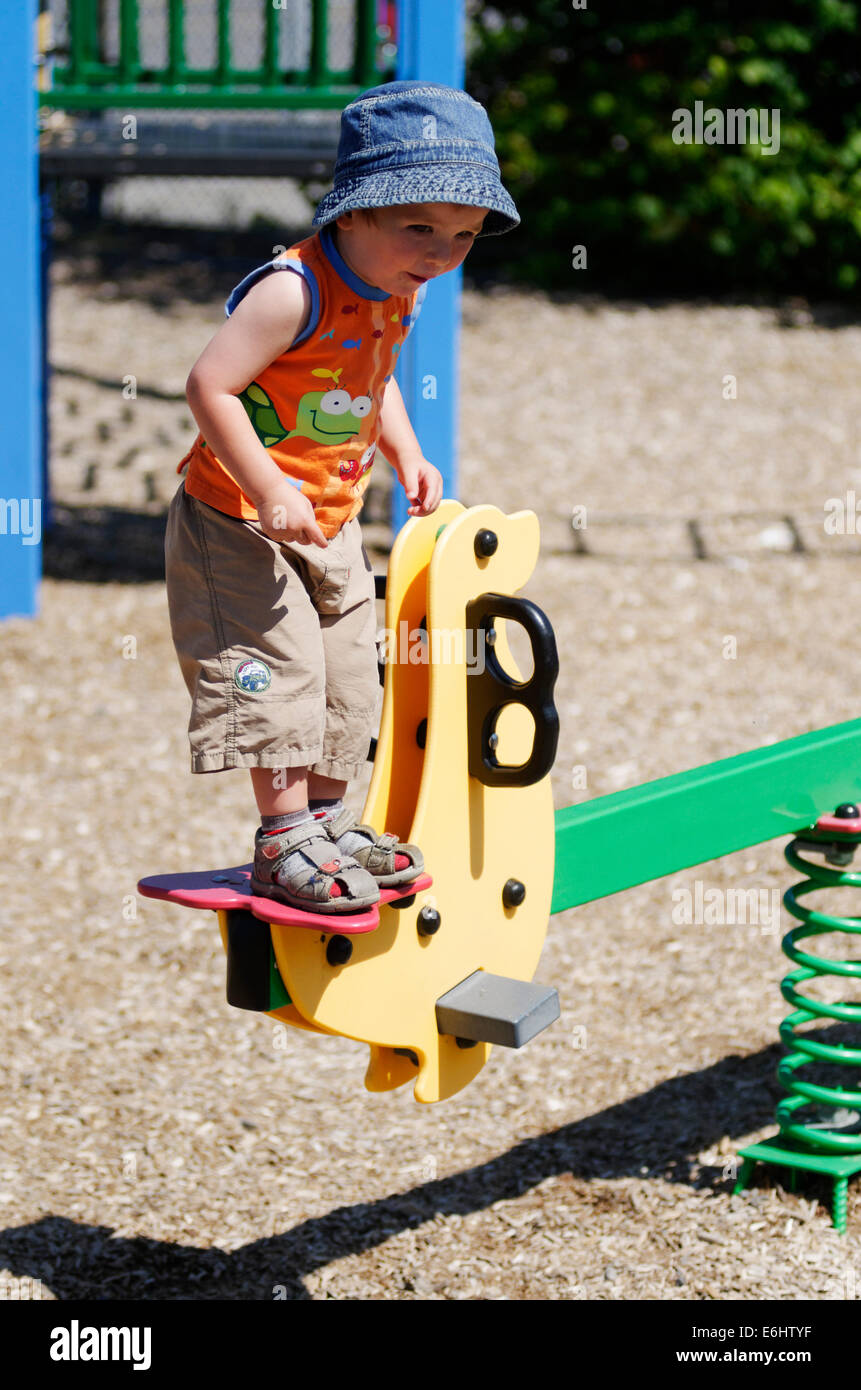 An excited young boy stood on a seesaw in a playground getting ready to ...
