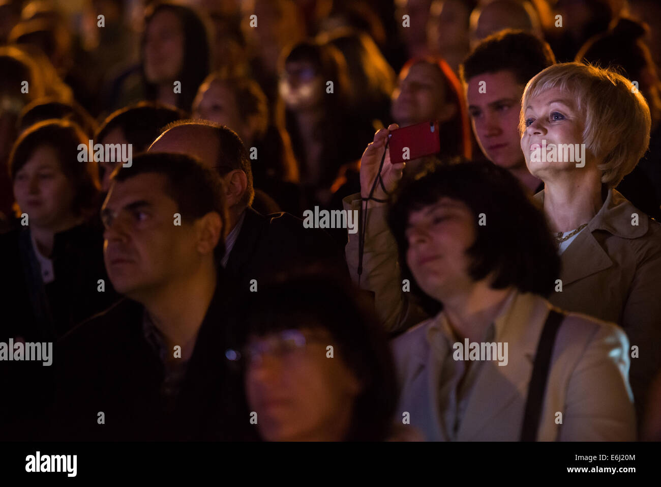 Group shot of outdoor sitting audience with focus on woman illuminated ...