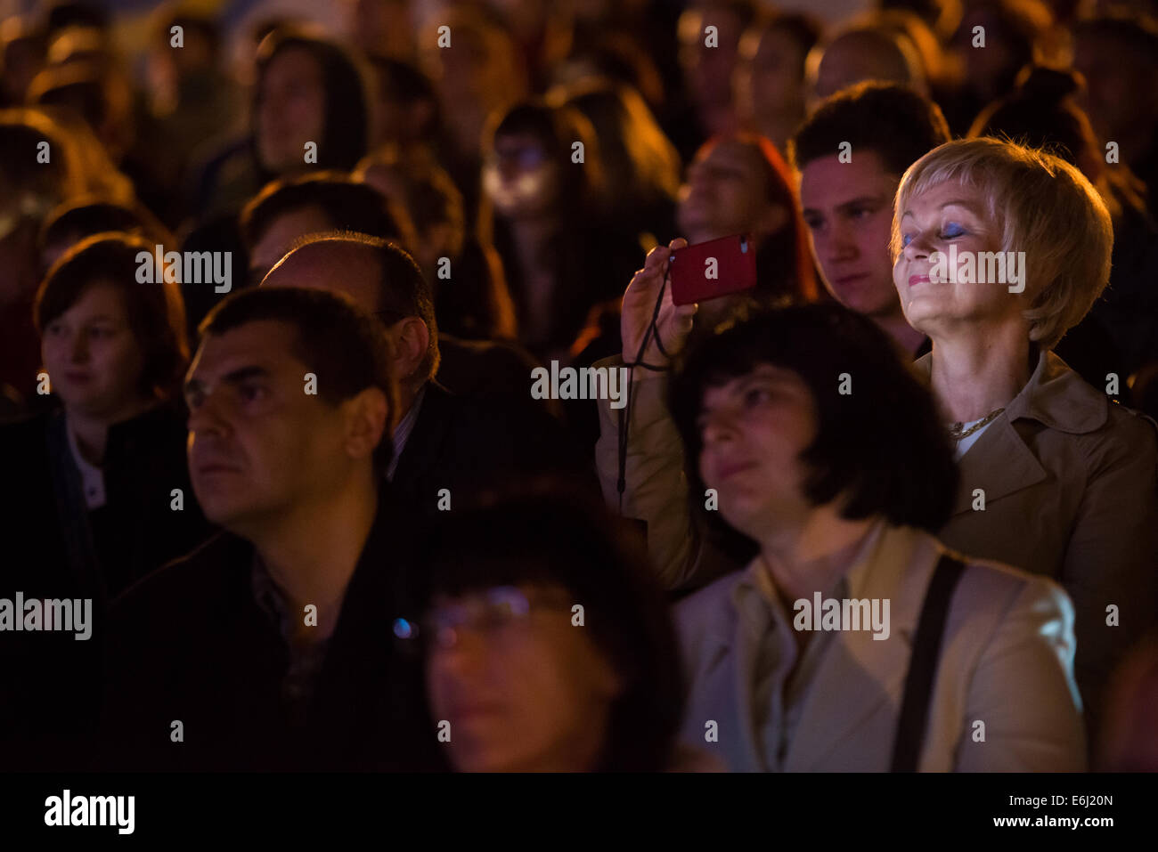 Group shot of outdoor sitting audience with focus on woman illuminated ...