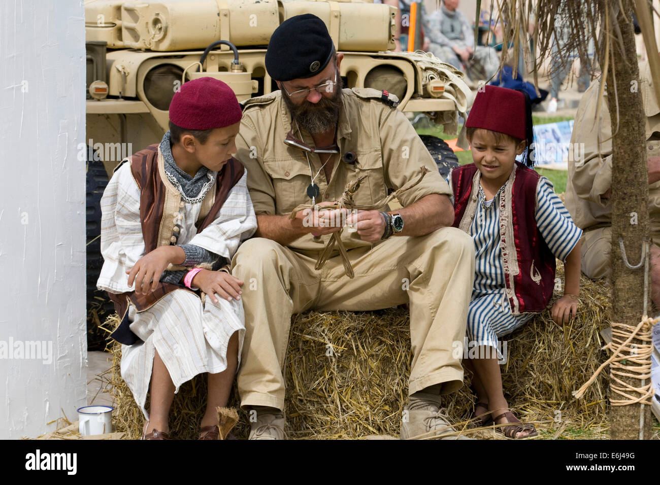 soldier making a reed Doll with traditionally dressed children watching ...