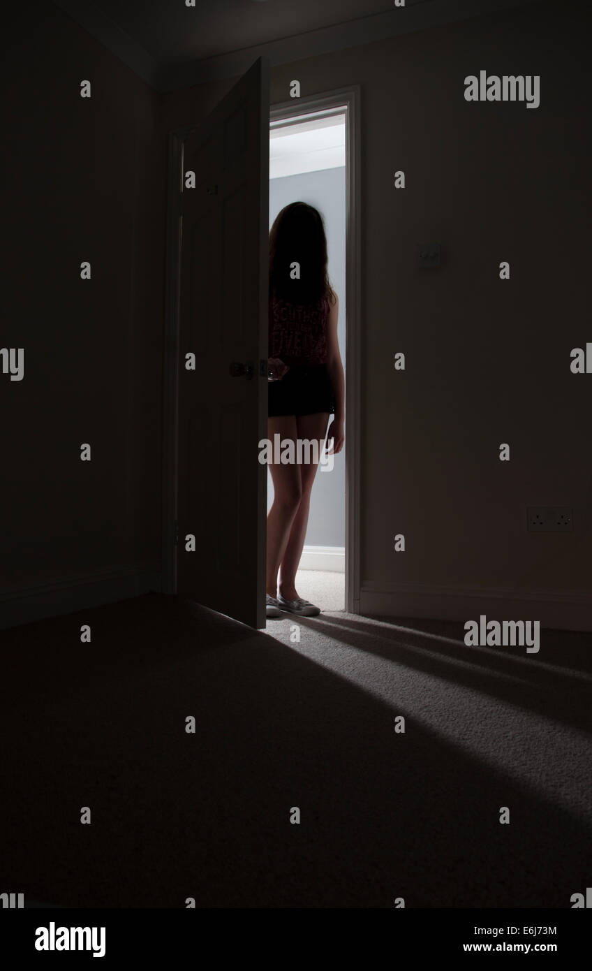Shadowy girl standing in a the doorway of darkened room, silhouette ...