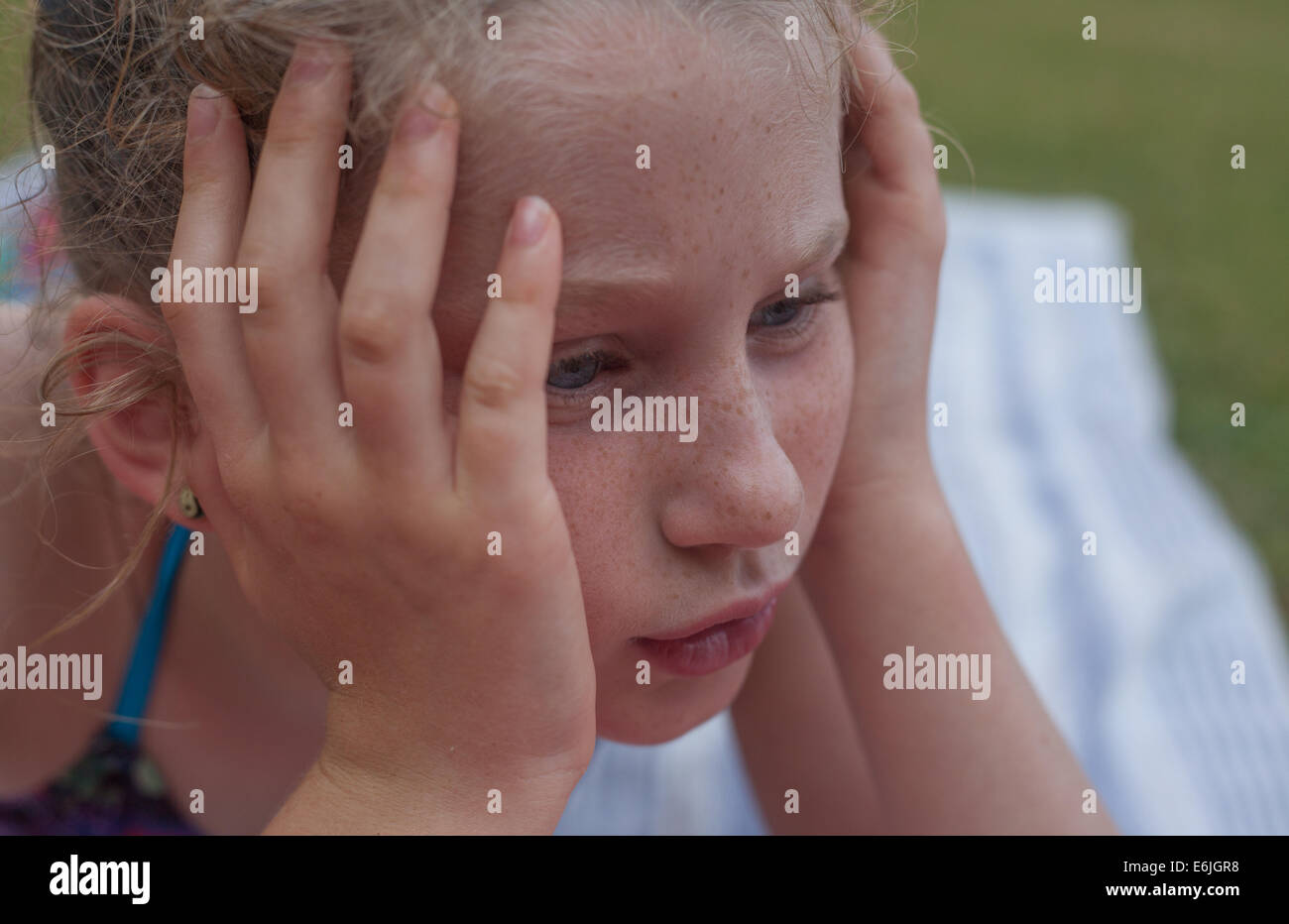 young girl hands up to face and looking bored or sad into distance ...