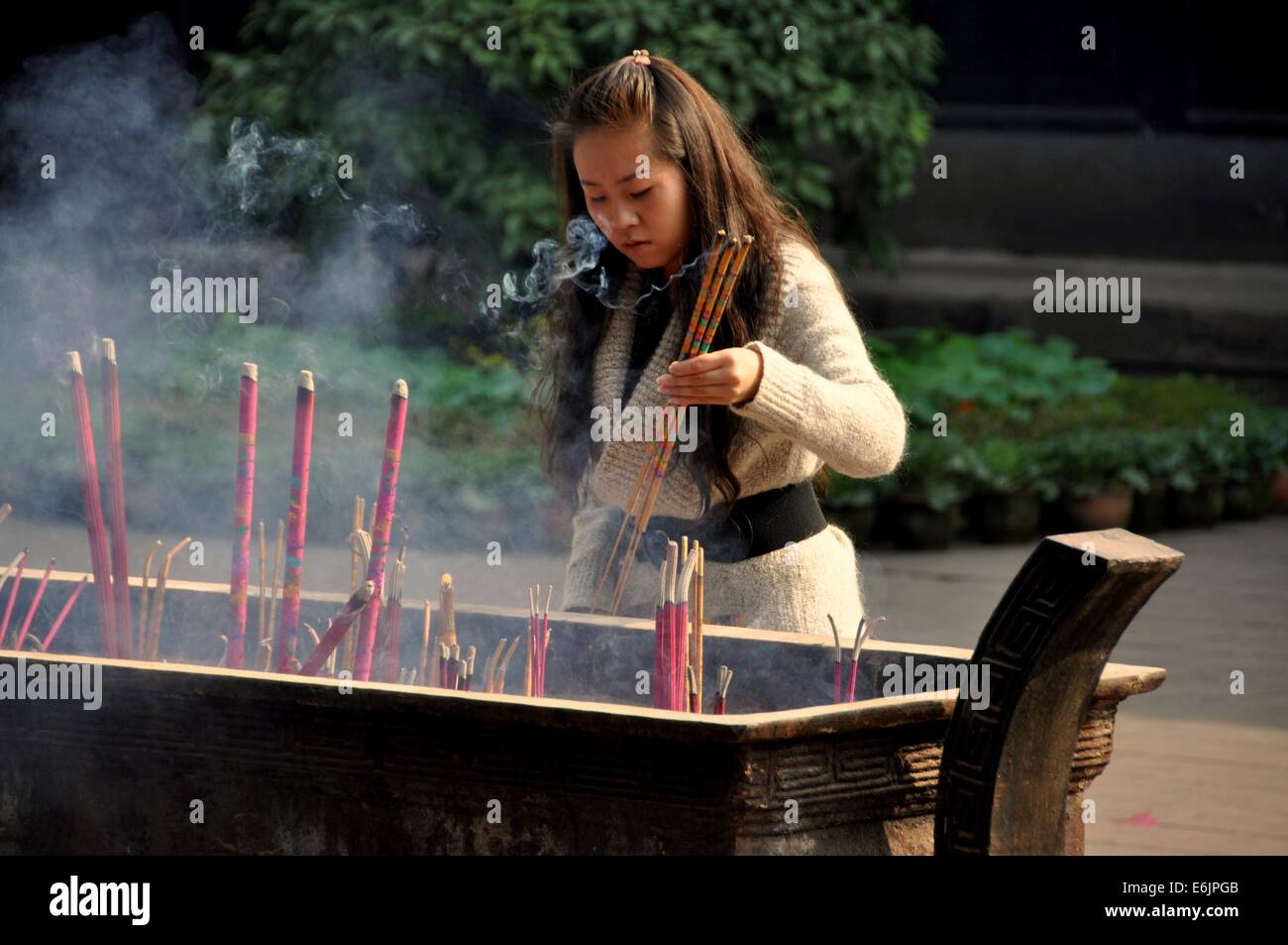 XINDU, CHINA: Young woman places three burning incense sticks into a ...