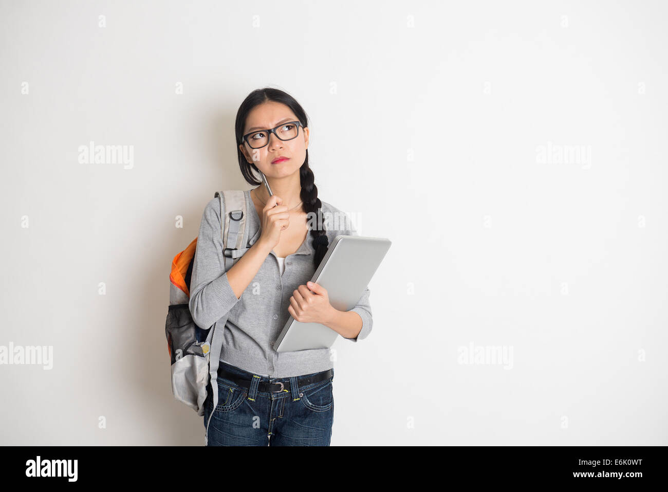 asian college girl thinking holding a pen with laptop on plain ...