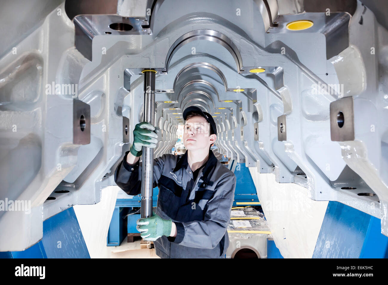 Employee fitting a tension rod into the engine frame of a marine engine ...