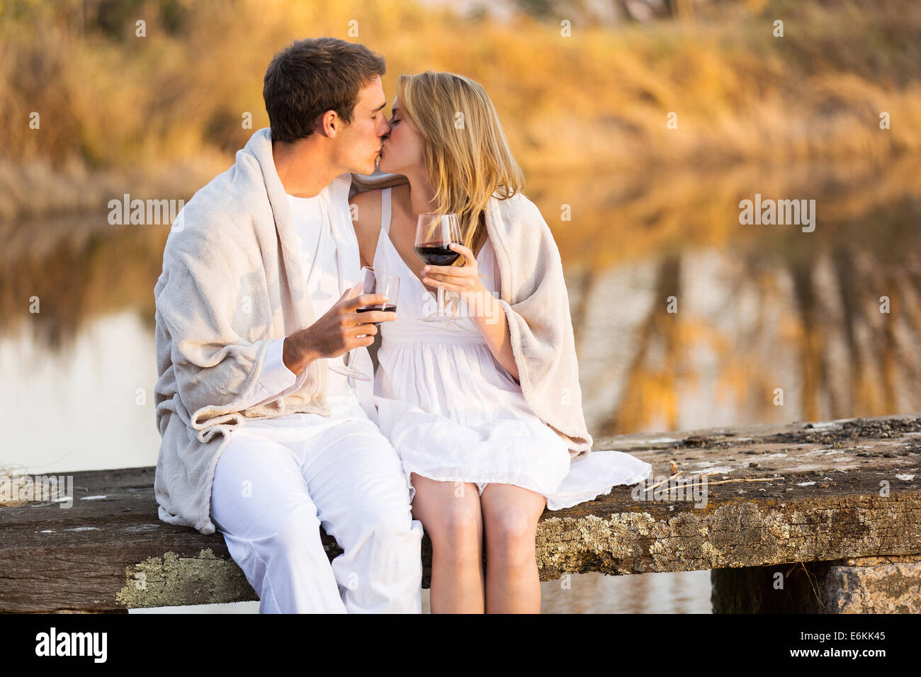 Romantic Couple Kissing On A Pier And Holding Glass Of Wine At Sunset
