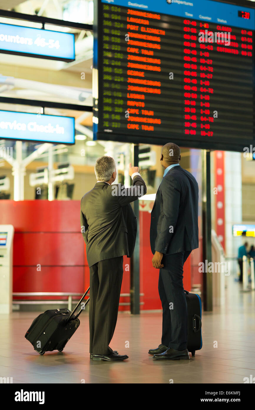 rear view of business partners checking flight information at airport ...