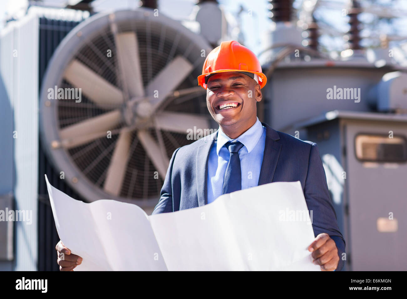 cheerful young African electrical manager holding blueprint in electric ...