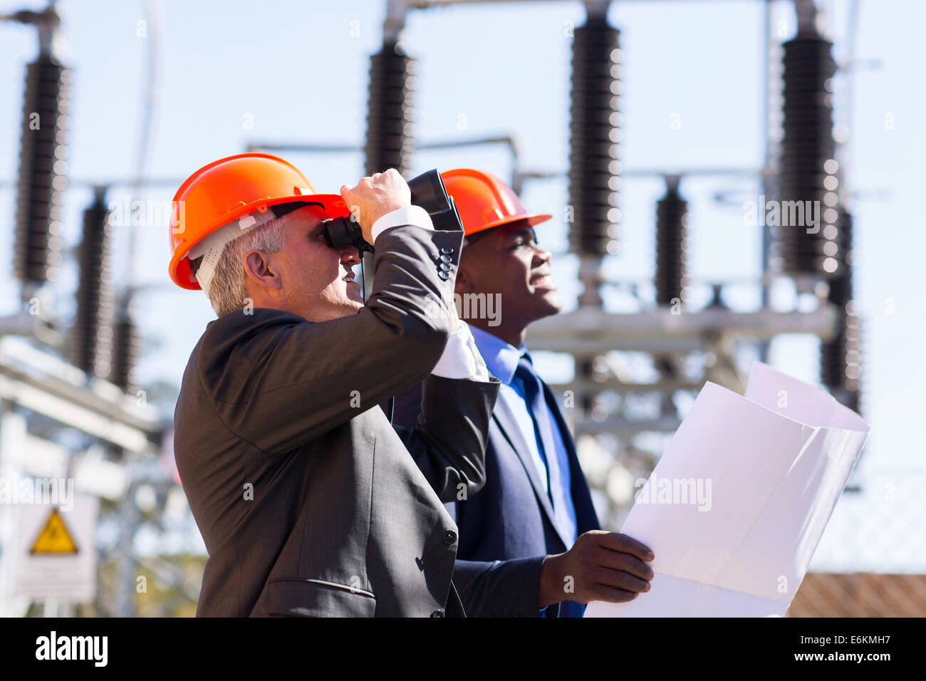 middle aged engineer and colleague with binoculars on electrical ...