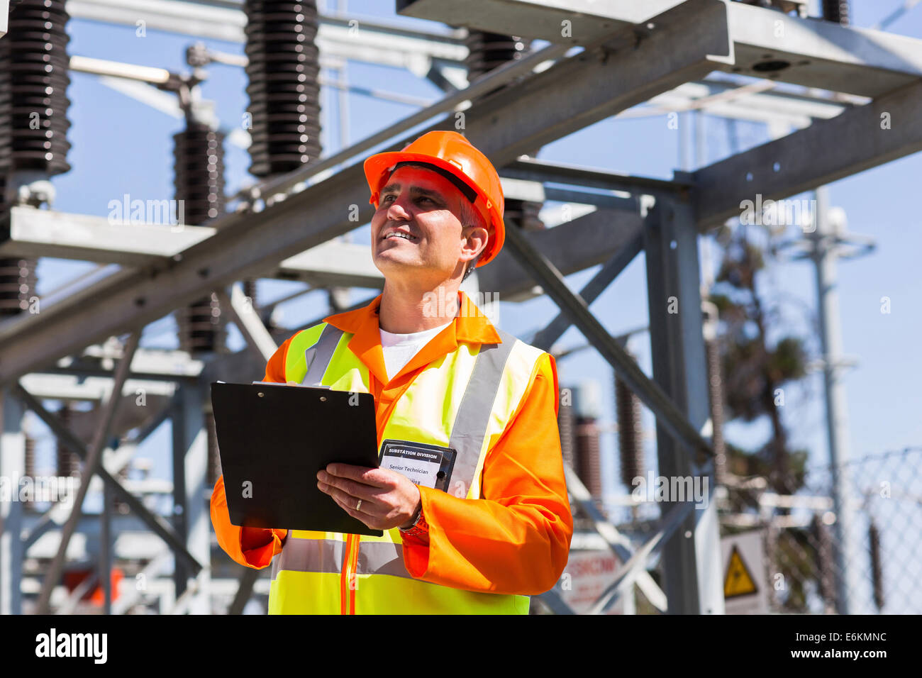 happy middle aged electrical engineer with clipboard in substation ...
