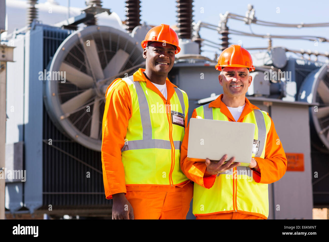 portrait of happy electrical engineers with laptop in front of ...
