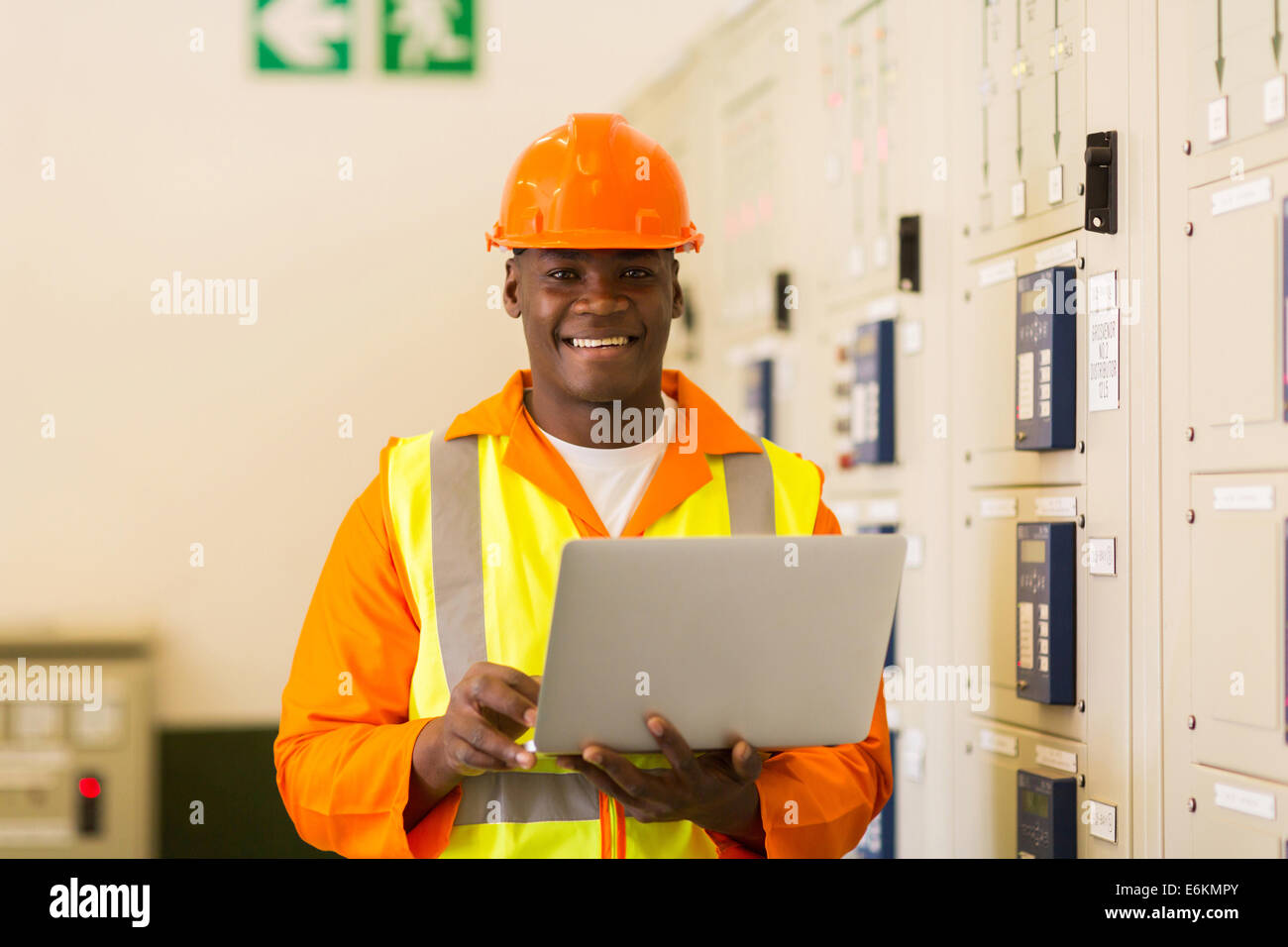 happy African electrical engineer with laptop computer in power plant ...