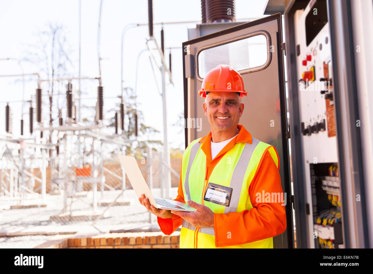 senior technician holding laptop in front of transformer at substation ...