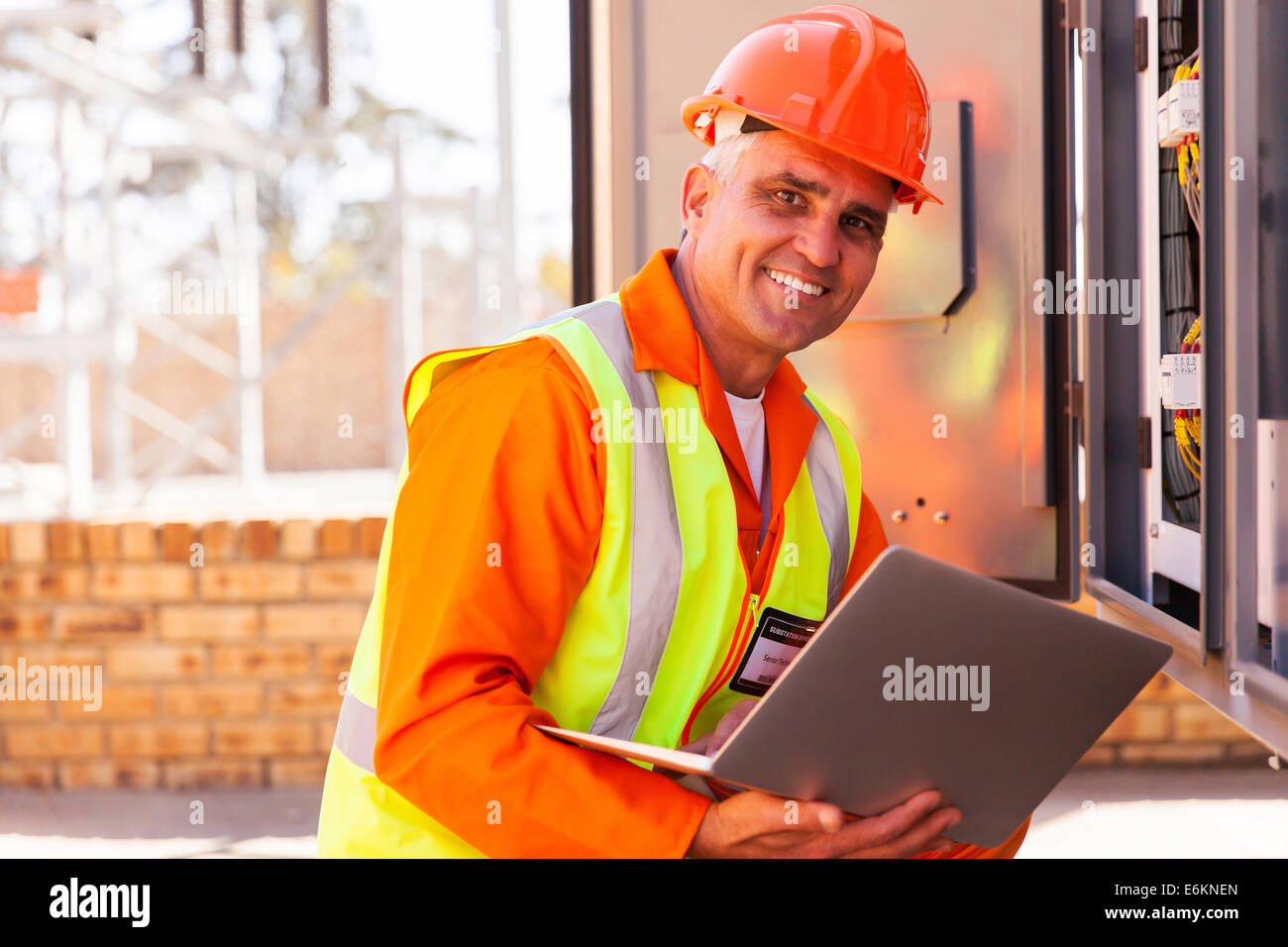 happy middle aged electrical engineer using laptop next to transformer ...