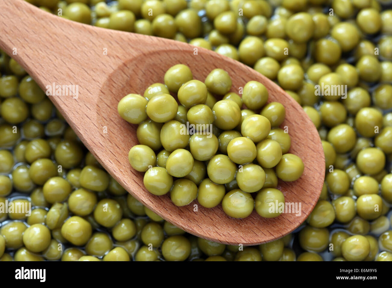 Preserved green peas in a wooden spoon on preserved green peas ...