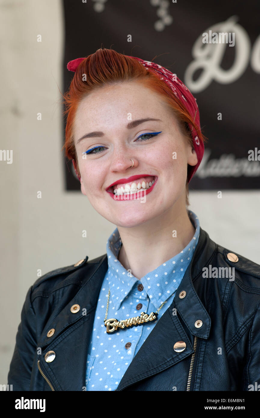 smiling young woman with red dyed hair attends to a stall at the ...
