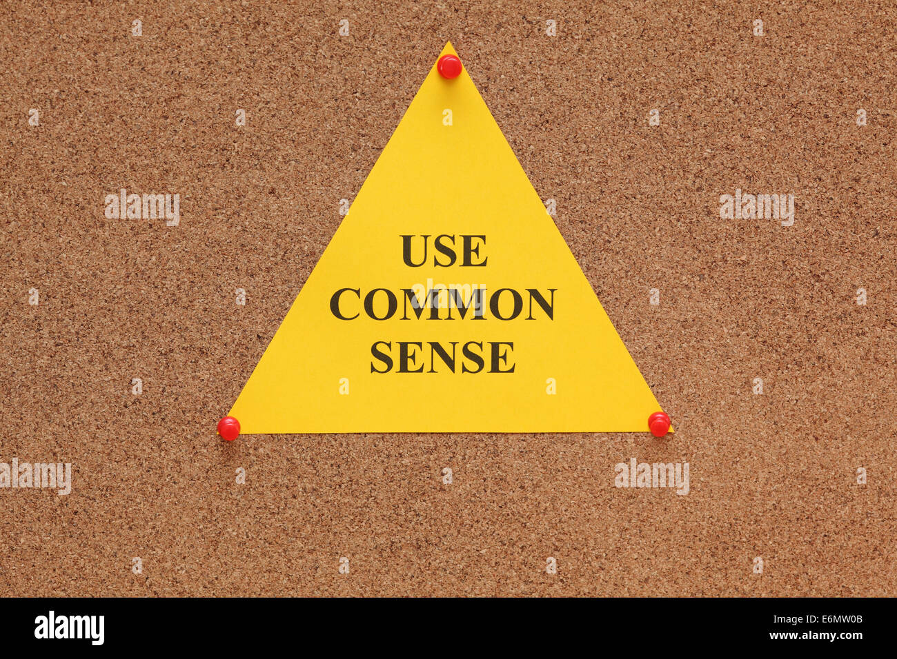 Triangular paper note with the words "use common sense" on cork board ...