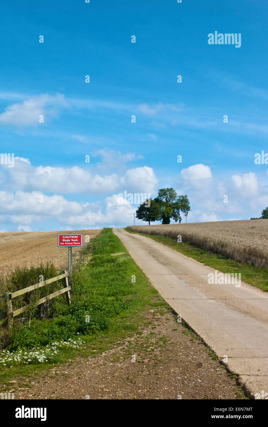 Farm track leading uphill through fields of crops. Red sign against ...