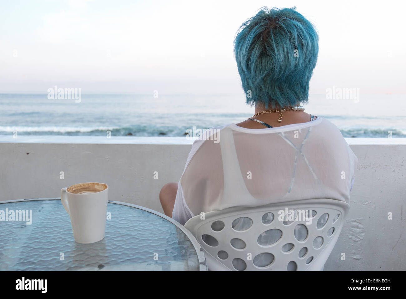 Woman sitting by a low wall with a cup of coffee looking out over the ...