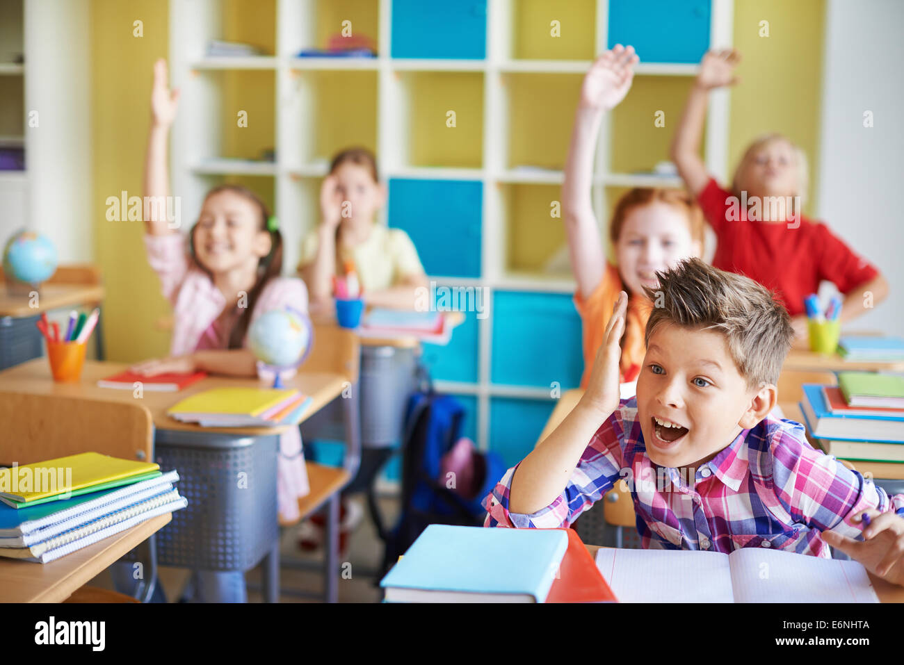 Clever schoolkids raising hands at workplaces during lesson Stock Photo ...
