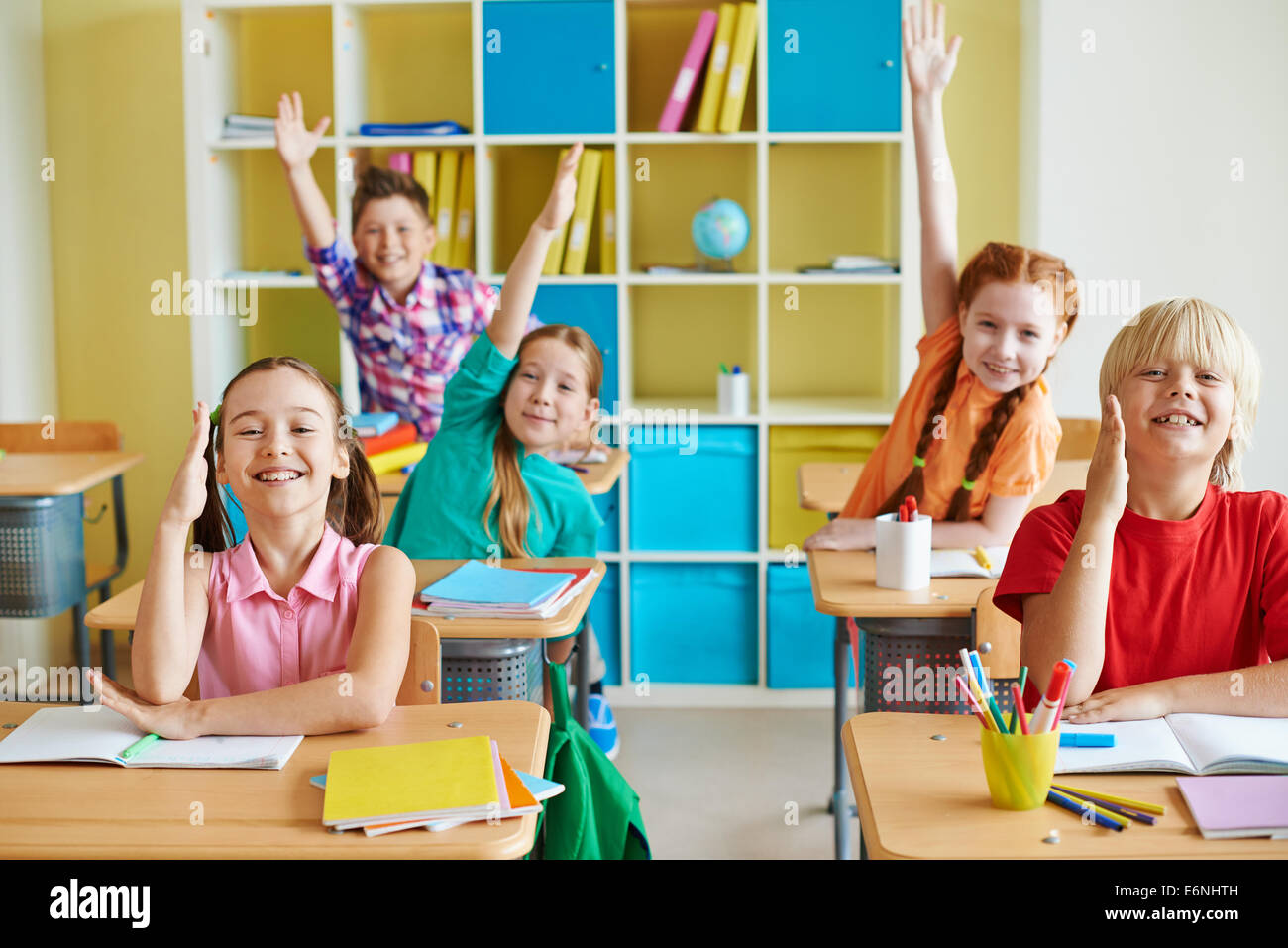 Happy classmates raising hands at lesson Stock Photo - Alamy