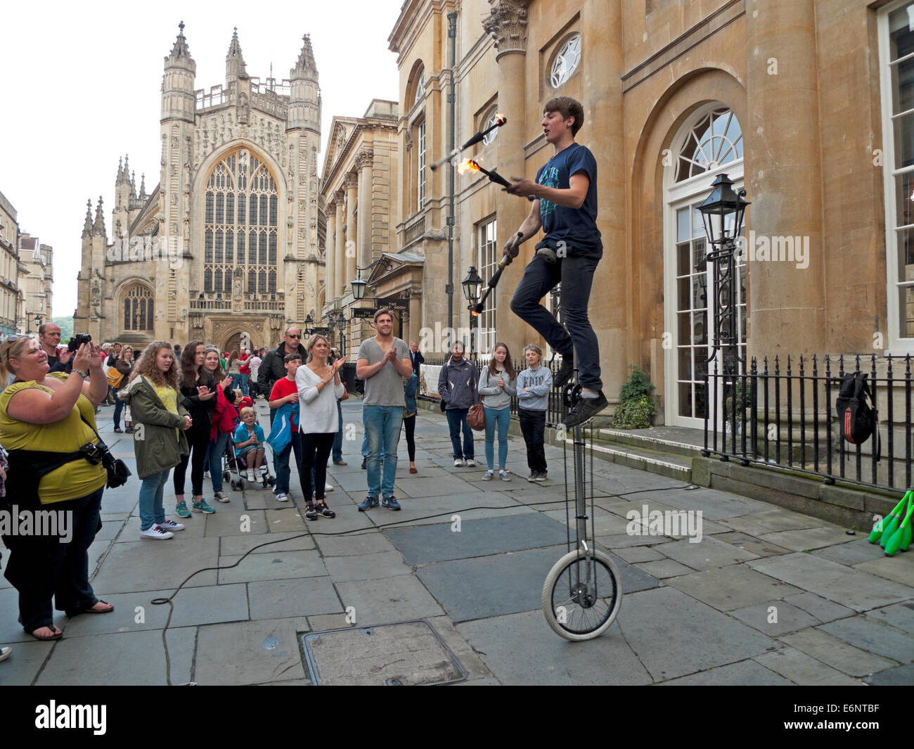 Street performer juggling with fire on a unicycle watched by tourists ...