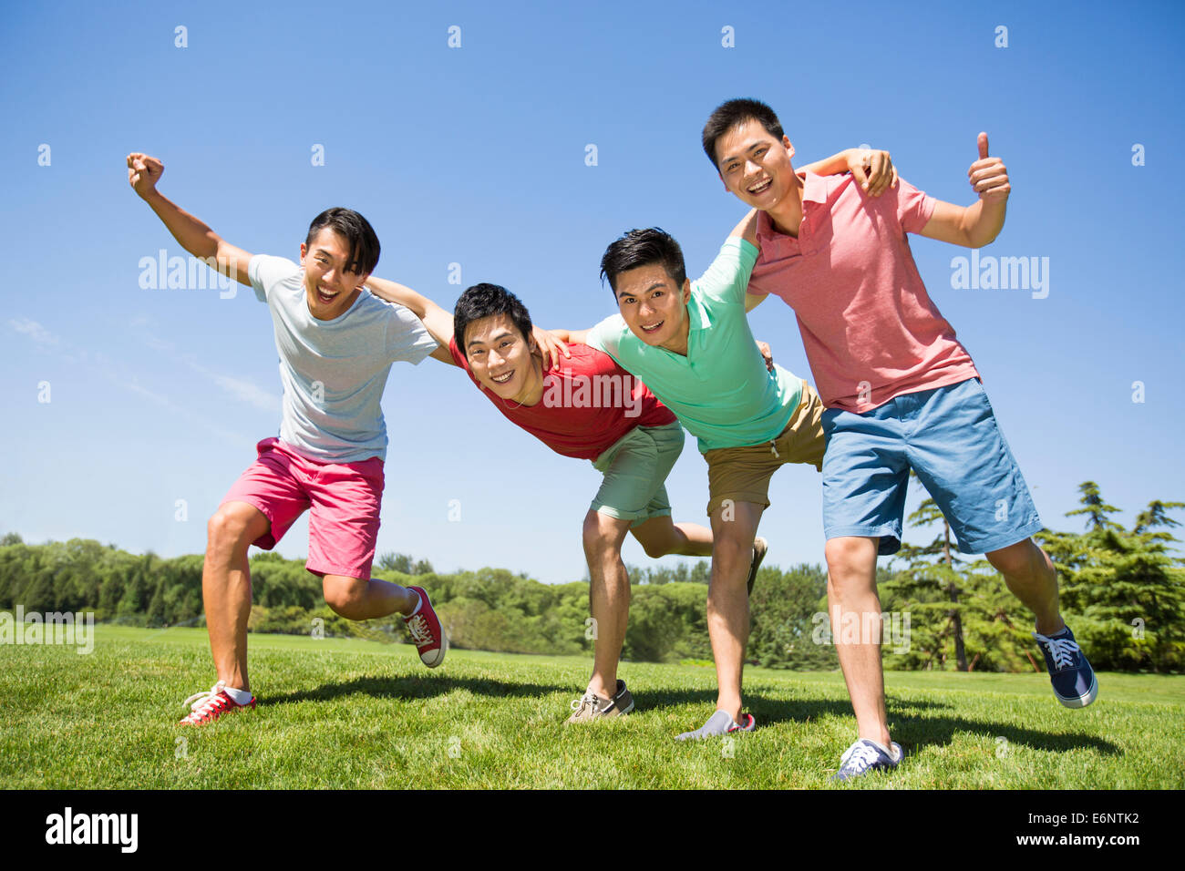 Four cheerful young men standing arm in arm on grass Stock Photo - Alamy