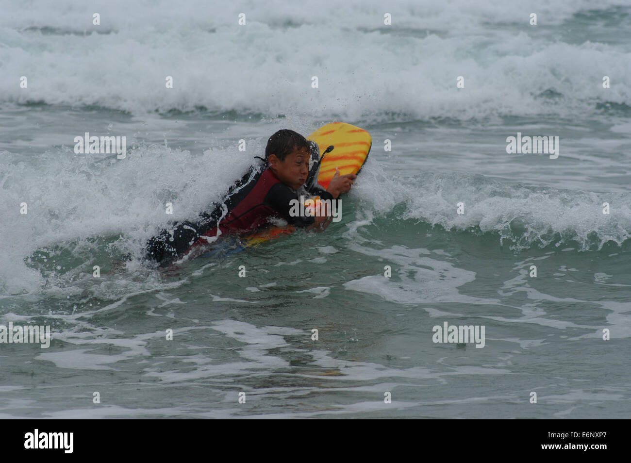 Young male teenager surfing on a bodyboard in the sea, paddling out ...